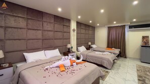 Quarto de hotel com duas camas, uma cabeceira grande acolchoada, um sonho apanhador pendurado na parede e um minibar.