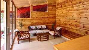 Um quarto aconchegante com paredes de madeira, um sofá, duas cadeiras e uma mesa de vidro.