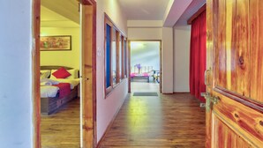 Um corredor com piso de madeira e portas, que leva a um quarto com cama e um quadro na parede.