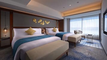Quarto de hotel com duas camas, área de estar e uma janela grande com cortinas.