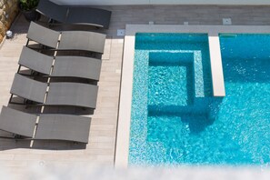 Uma piscina com borda azulejada, rodeada por espreguiçadeiras e um deck revestido de azulejos.