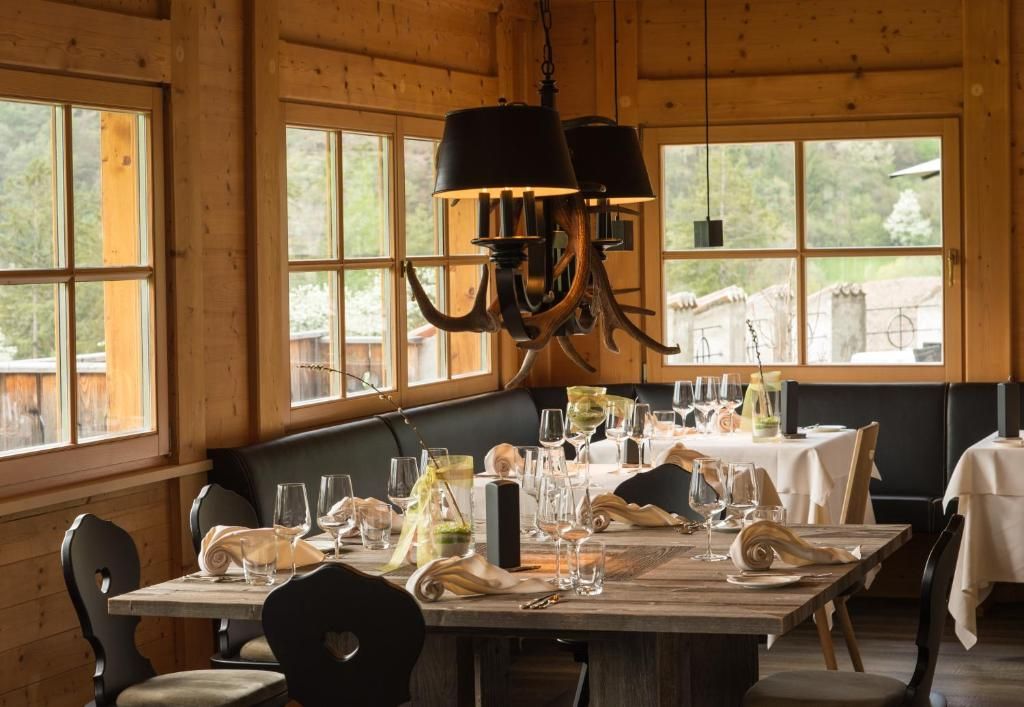 Uma área de refeições com mesa de madeira posta para uma refeição, um candelabro e grandes janelas com vista para o verde.