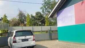 Um carro branco estacionado numa área pavimentada, com um edifício ao fundo, que apresenta uma parede grande e colorida.