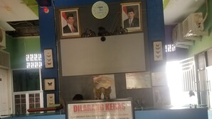 Uma área de recepção com balcão azul, fotos emolduradas, um relógio e uma placa com texto.