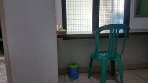 Um quarto com janela, uma cadeira de plástico verde e uma lixeira azul.
