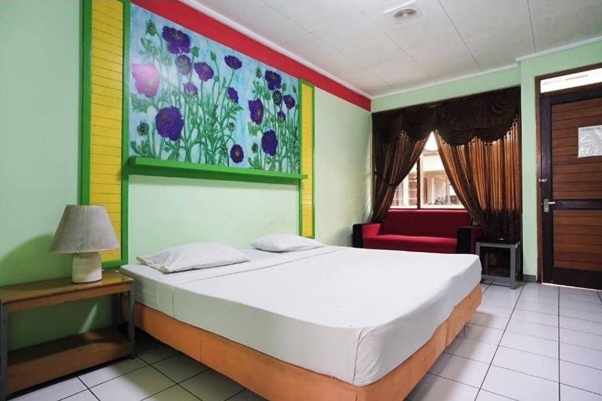 Um quarto com cama, mesa de cabeceira, sofá vermelho e um quadro na parede.