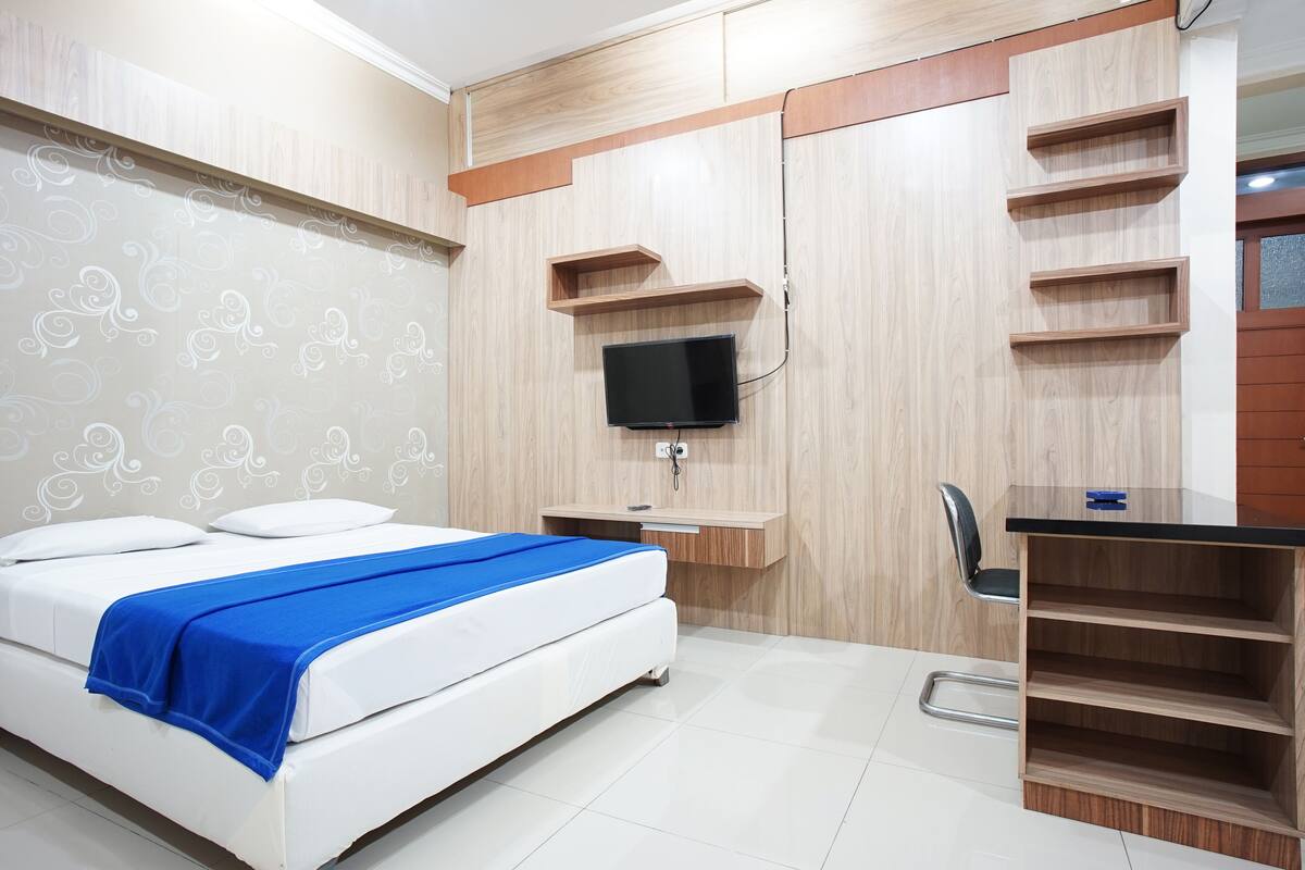 Quarto de hotel moderno com cama, TV fixada na parede e prateleiras embutidas.