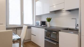 Cozinha moderna com armários brancos, eletrodomésticos de aço inoxidável e uma janela que proporciona iluminação natural.