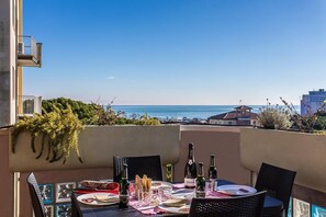 Mesa de varanda posta com pratos, copos e garrafas, com vista para a costa.