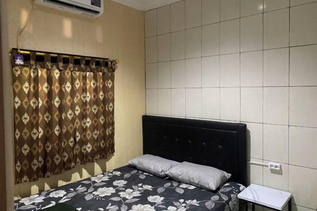 Um quarto com uma cama, uma janela com cortinas estampadas e uma parede revestida de azulejos.