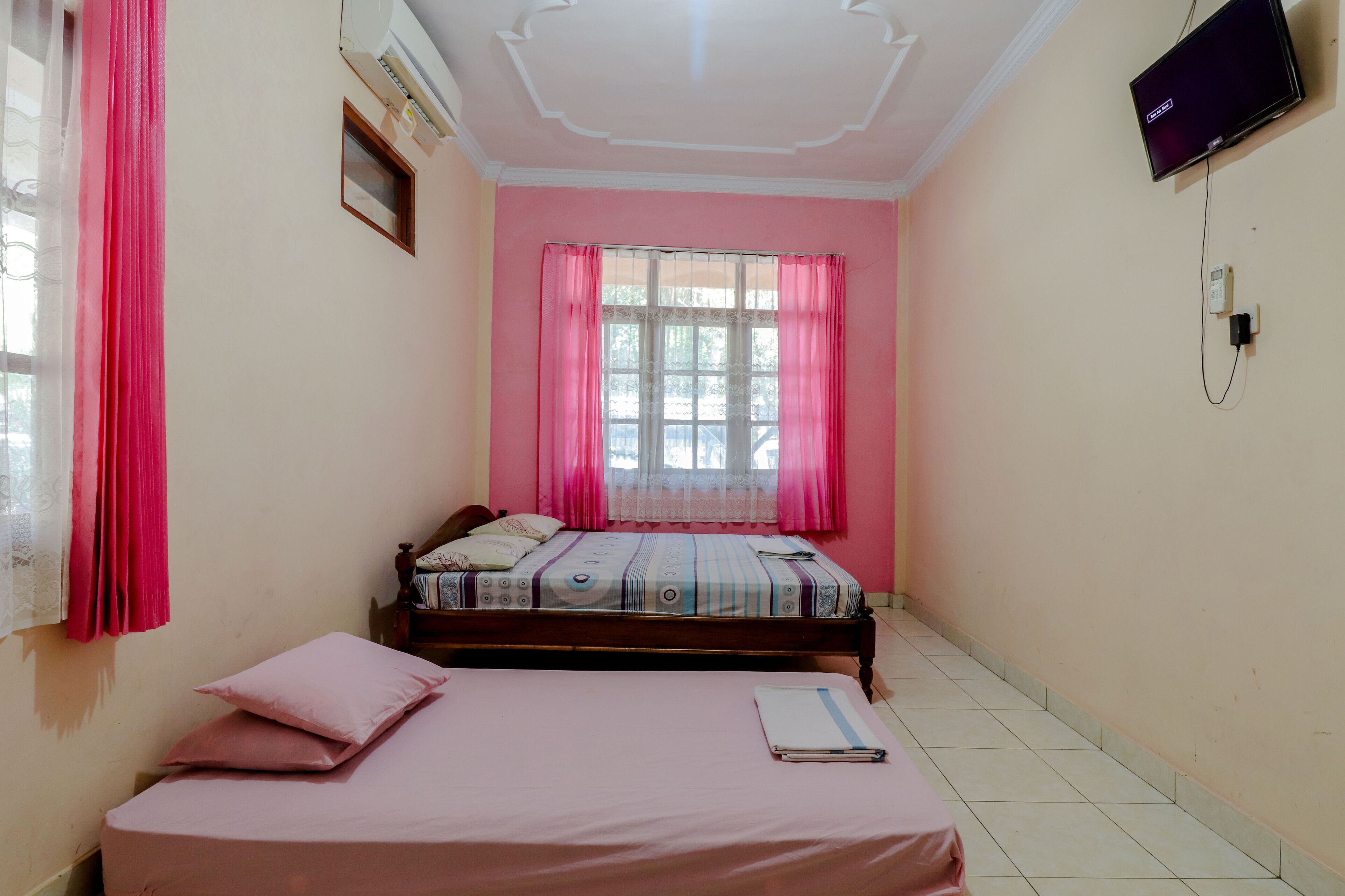 Quarto com cama, mesa de cabeceira, televisão e janela com cortinas.