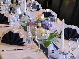 Mesa posta para uma ocasião de jantar formal, com copos de vidro transparente, uma vela branca e arranjos florais.