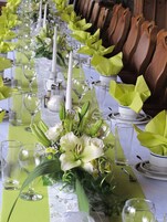 Uma mesa de jantar comprida posta com toalhas verdes, louça branca e arranjos florais.