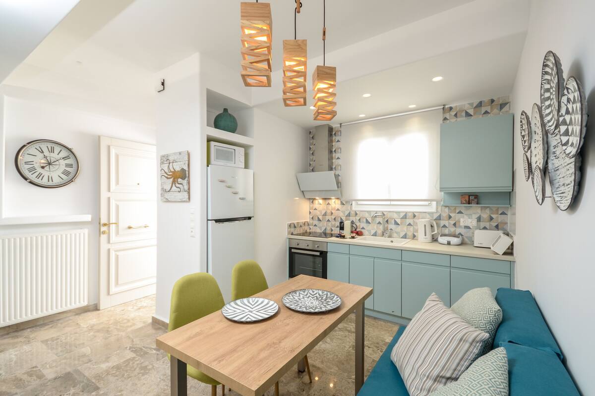 Cozinha moderna com área de refeições, apresentando uma mesa de madeira, cadeiras verdes e um sofá azul.