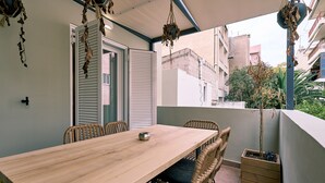 Uma mesa de jantar de madeira com cadeiras, uma planta pendurada e um vaso com planta numa varanda.