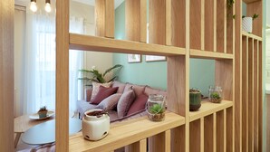 Quarto com divisória de madeira, sofá com almofadas, mesa pequena com planta e luminária pendente.