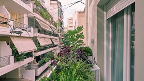 Um corredor externo estreito com várias varandas, algumas com plantas e mobiliário de exterior.