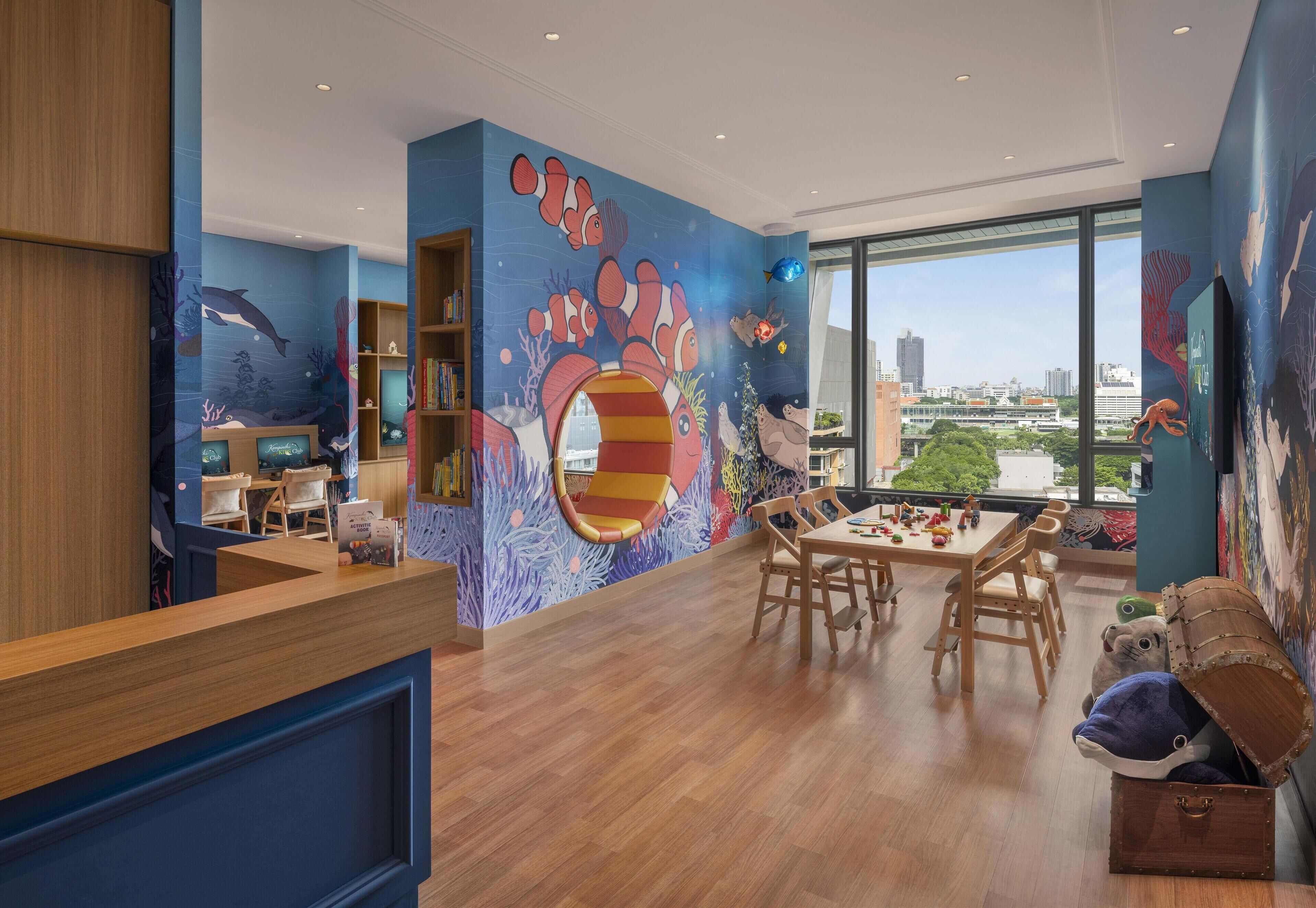 Espaço infantil com um grande mural, mobiliário de madeira e vista para a cidade.