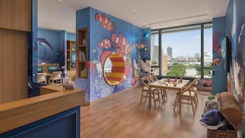 Espaço infantil com um grande mural, mobiliário de madeira e vista para a cidade.