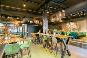 Um restaurante moderno com área de bar, cadeiras e sofá verdes.