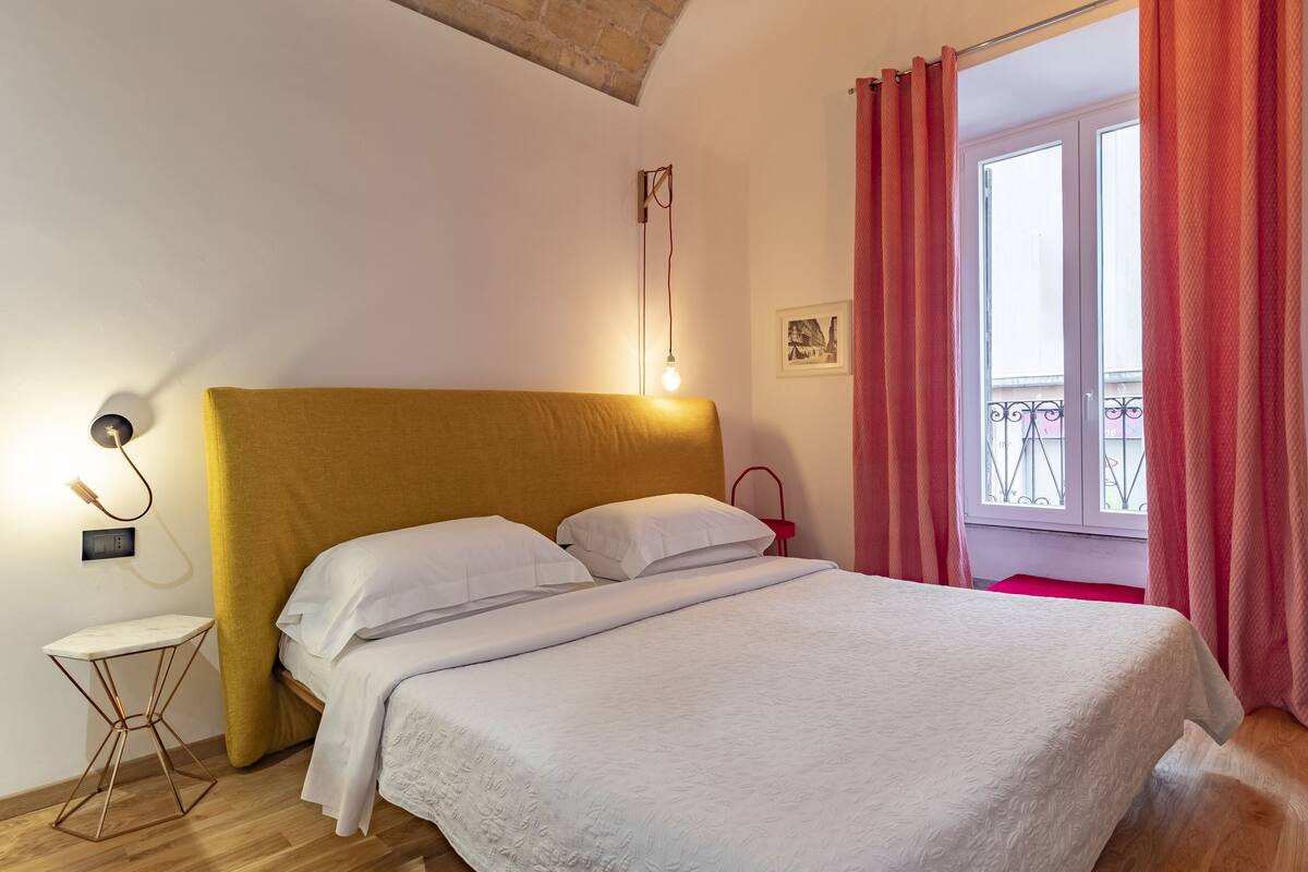 Cama bem arrumada com lençóis brancos, cabeceira de madeira e mesa de cabeceira com abajur.