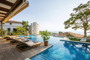 Uma área à beira da piscina com espreguiçadeiras, uma planta em vaso e vista para o mar.
