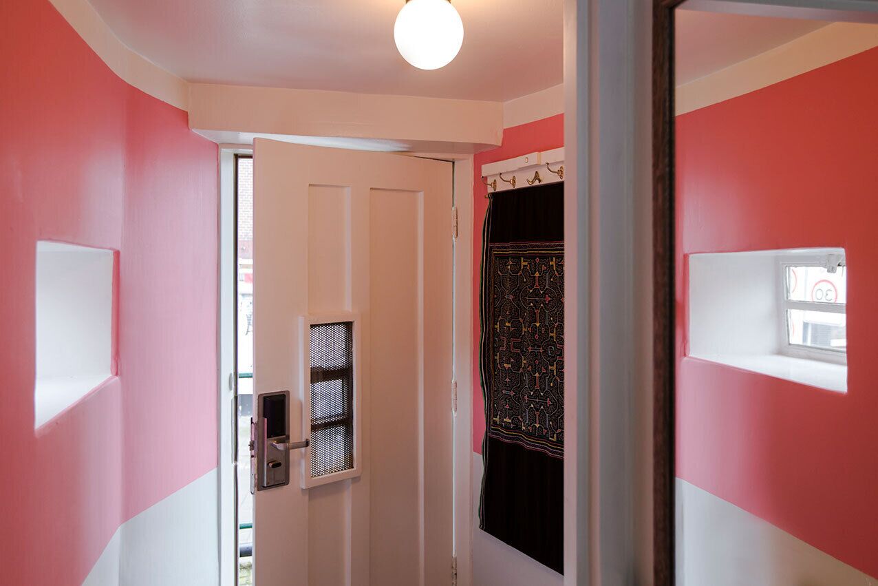 Um corredor com paredes cor-de-rosa, uma porta branca e uma janela com cortina.