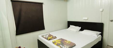 Um quarto com uma cama, um ventilador de teto, um ar condicionado, uma janela com persiana e uma mesa pequena com um vaso de flores.