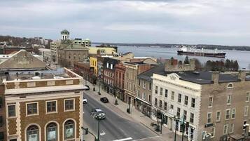 Uma rua urbana com edifícios históricos, um rio e um navio grande à distância.
