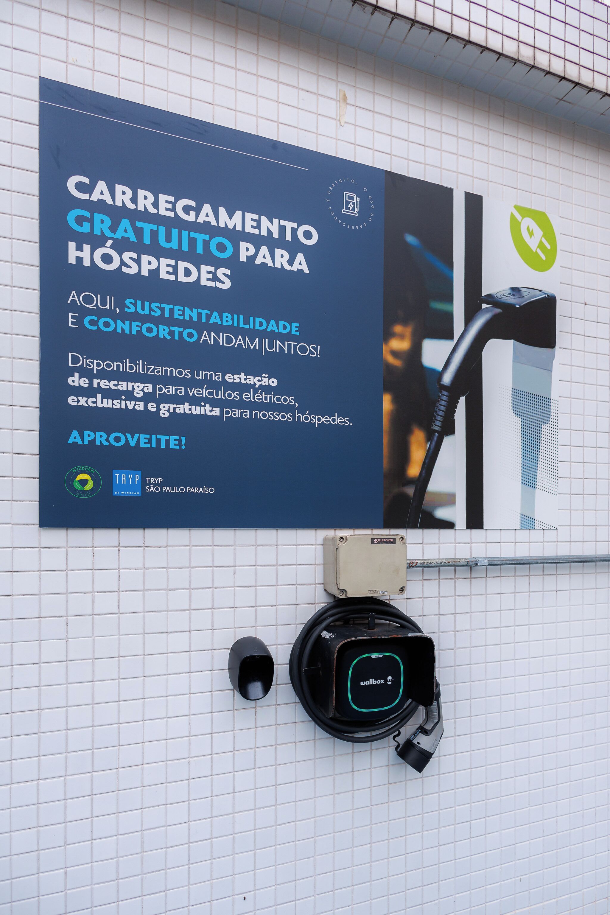 Publicidade na parede sobre carregamento gratuito para veículos elétricos, uma estação de carregamento e o logotipo da Tryp São Paulo Paraíso.