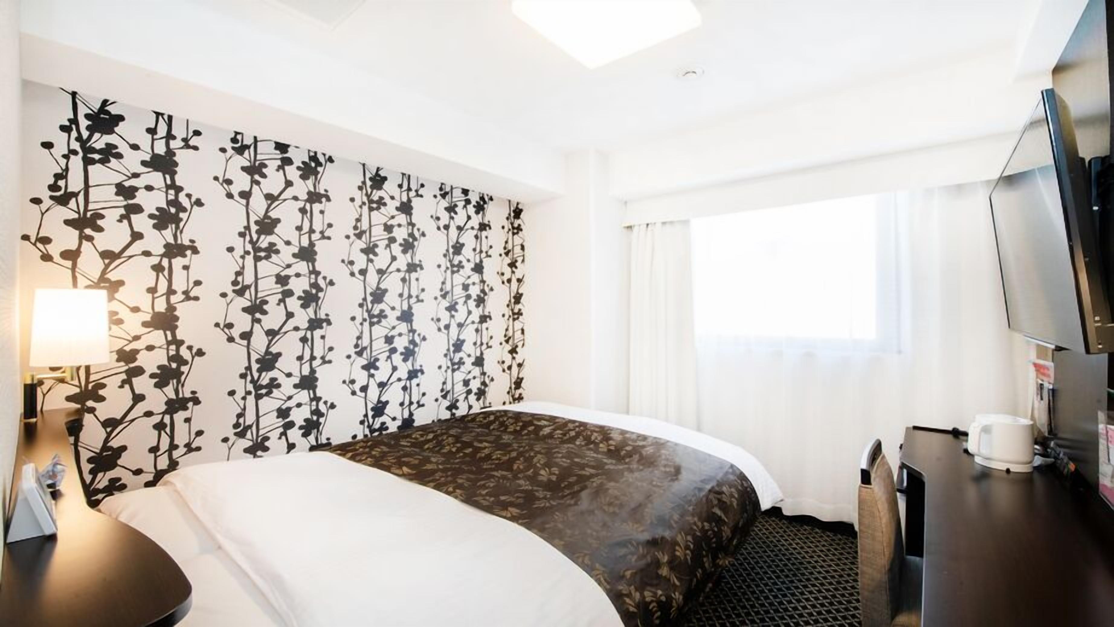 Quarto de hotel com cama, escrivaninha, televisão e janela com cortinas.