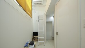 Um corredor estreito com parede branca, uma prateleira de madeira com toalhas, uma escada e uma televisão.
