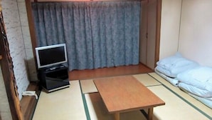 Um quarto pequeno com tatames, uma televisão, uma cama e uma mesa de madeira.
