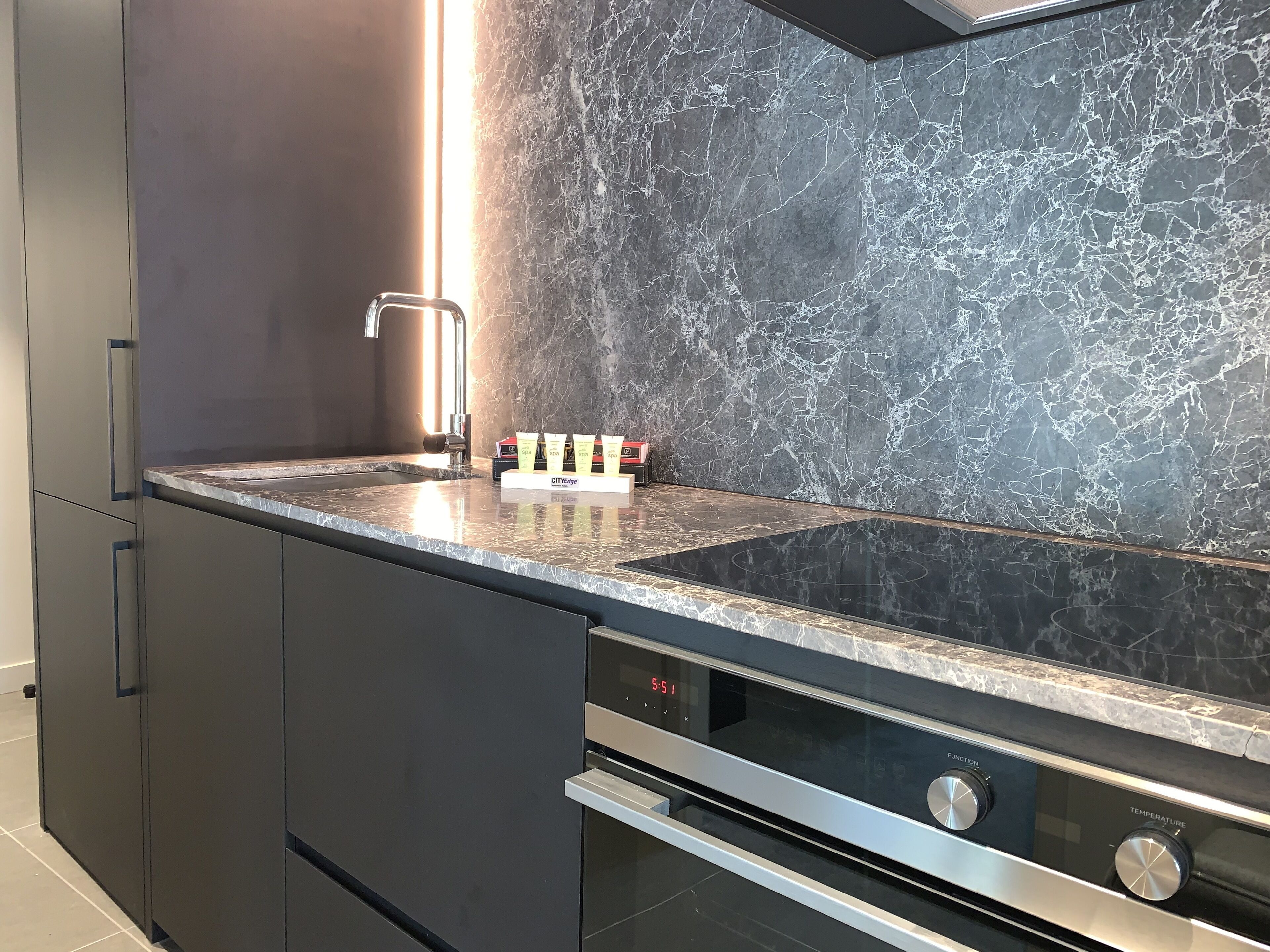Cozinha moderna com painel de mármore escuro, eletrodomésticos de aço inoxidável e forno embutido.