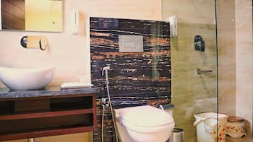 Um banheiro com painel de parede de mármore, pia branca, vaso sanitário, chuveiro e espelho.