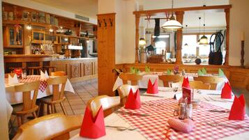 Restaurante com móveis de madeira, toalhas de mesa quadriculadas em vermelho e branco e suportes de guardanapo vermelhos.