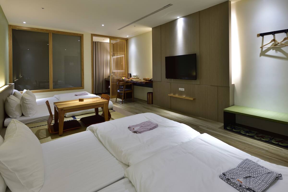 Quarto de hotel com duas camas, uma escrivaninha, televisão e porta de correr para uma varanda.