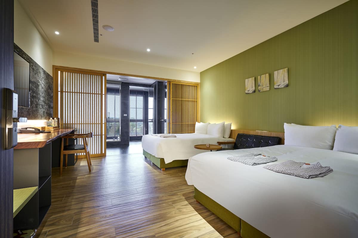 Quarto de hotel com duas camas, uma mesa de trabalho e vista para o exterior.