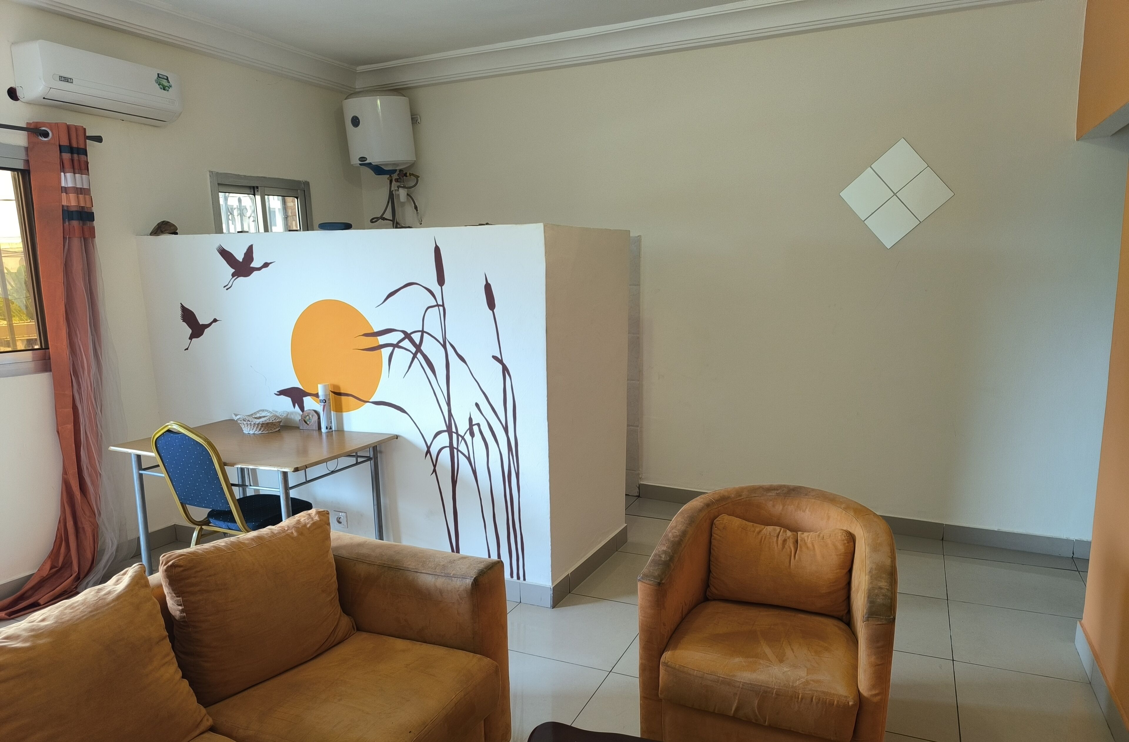 Sala de estar com sofá, uma poltrona, uma mesa e parede decorativa com um sol e pássaros.