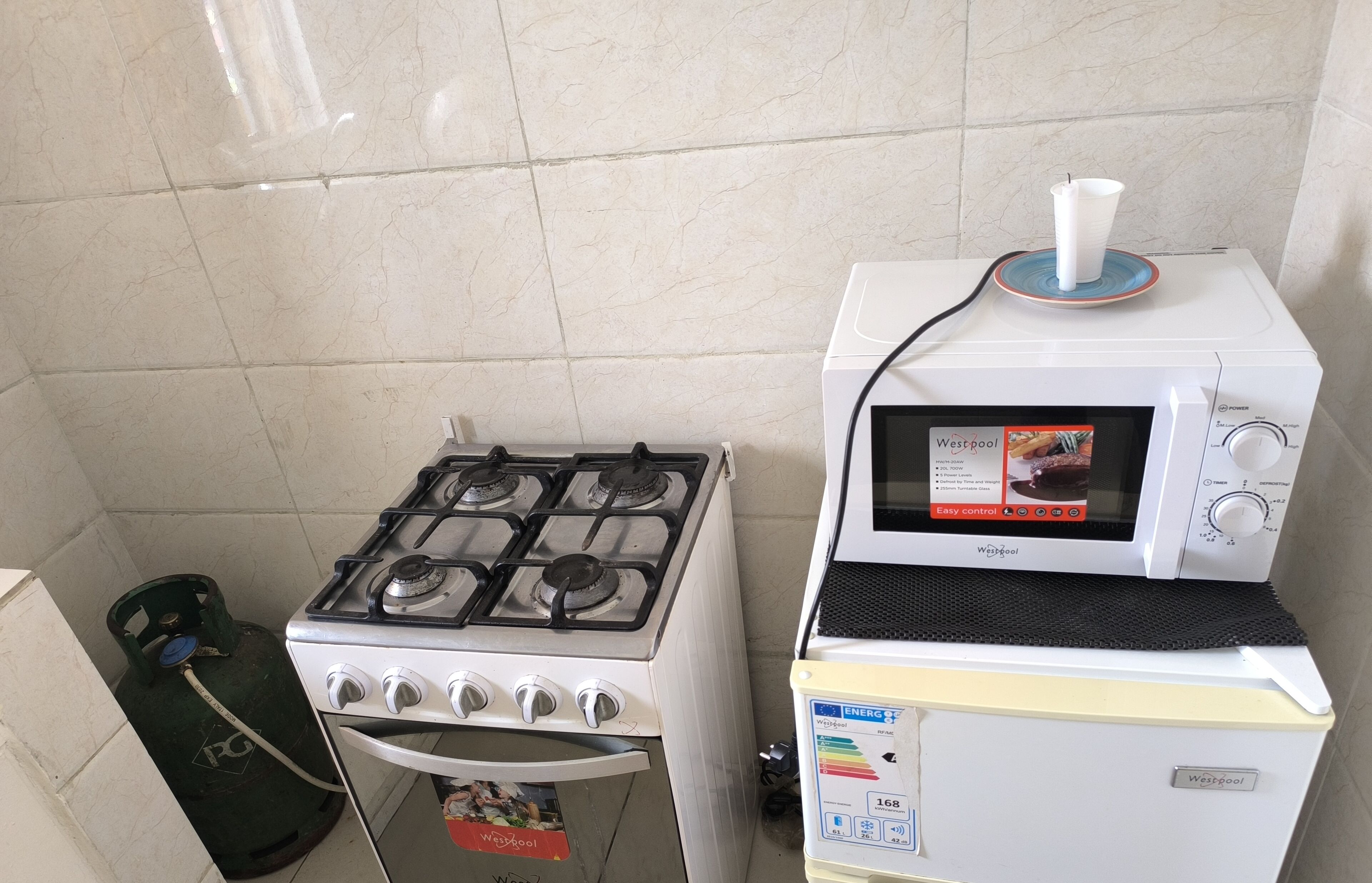 Uma cozinha com fogão a gás, micro-ondas Westpool e frigorífico Westpool.
