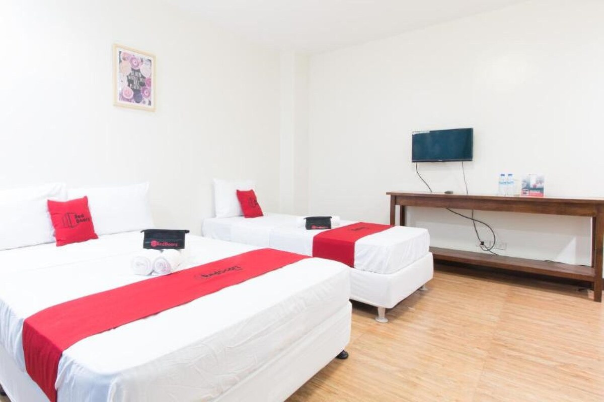 Quarto de hotel com duas camas, uma televisão e uma mesinha.