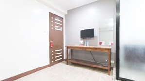Quarto com uma escrivaninha de madeira, uma televisão na parede e uma porta com extintor de incêndio.