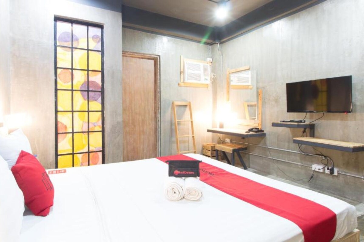 Quarto de hotel com cama, secretária e cadeira, televisão e janela com vista.