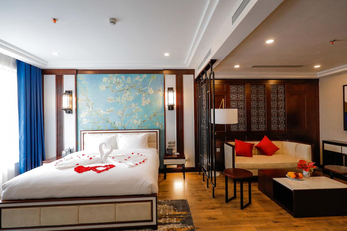Quarto de hotel com uma cama grande, um sofá, uma mesa de centro e uma parede decorativa com padrão floral.