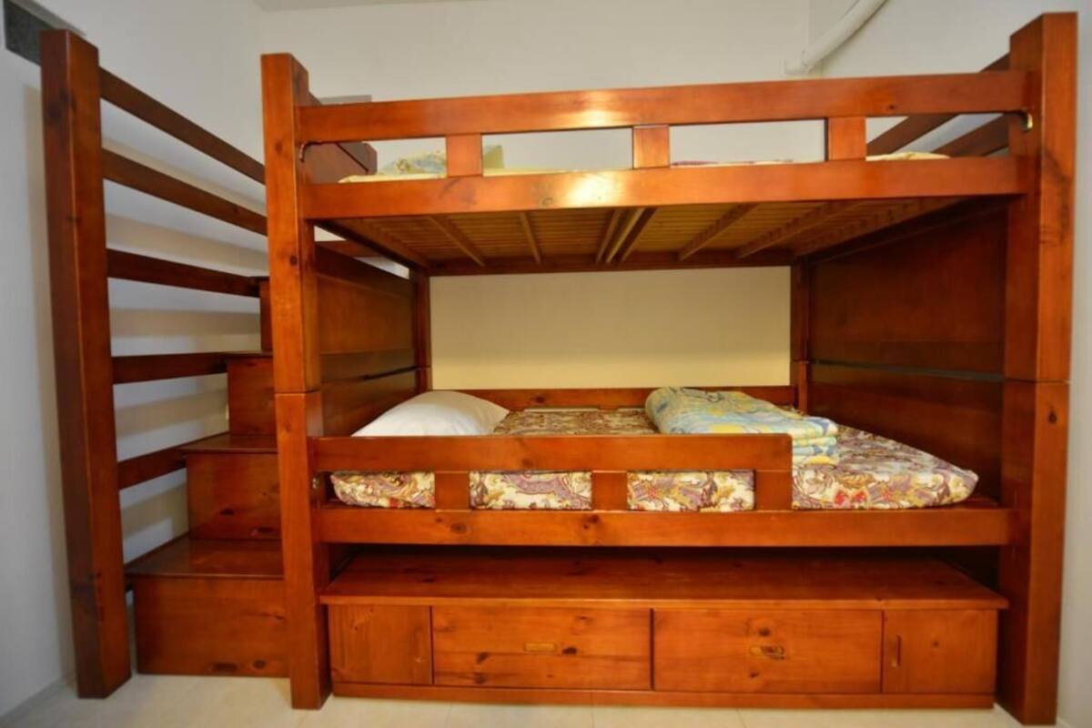 Uma cama de solteiro com estrutura de madeira, um colchão com roupa de cama estampada e uma prateleira inferior com gavetas.