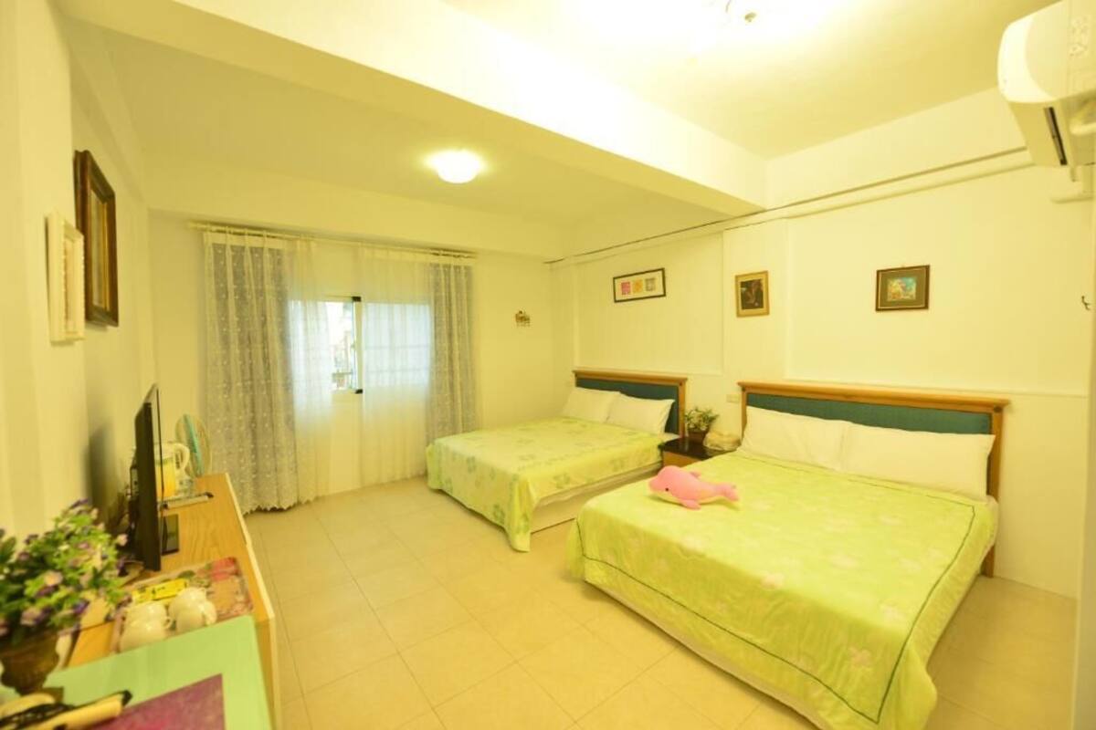 Quarto de hotel com duas camas, uma secretária com computador e uma janela com cortinas.