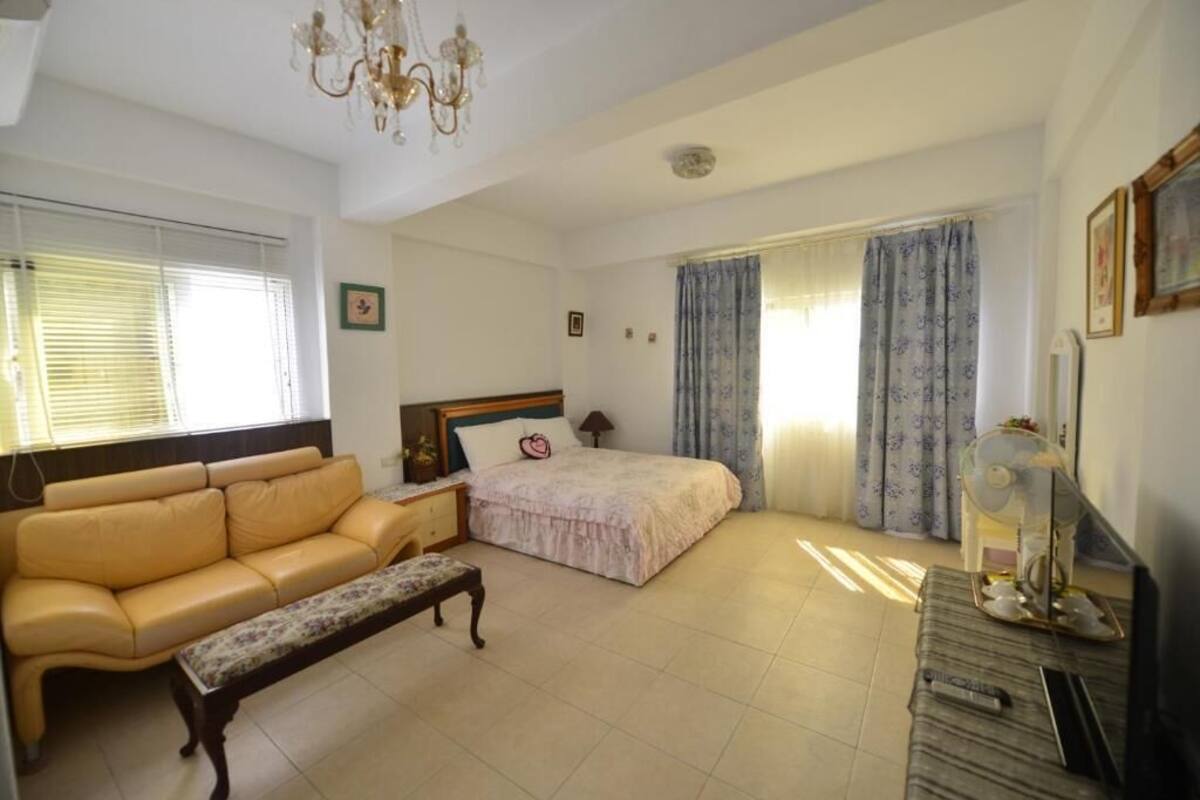 Um quarto com cama, sofá, banco, cômoda e lustre.