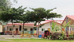 Um edifício com telhado vermelho e várias janelas, cercado por vegetação e áreas de estar ao ar livre.