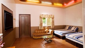 Quarto compacto com sofá, duas camas de solteiro, televisão e janela com cortinas.