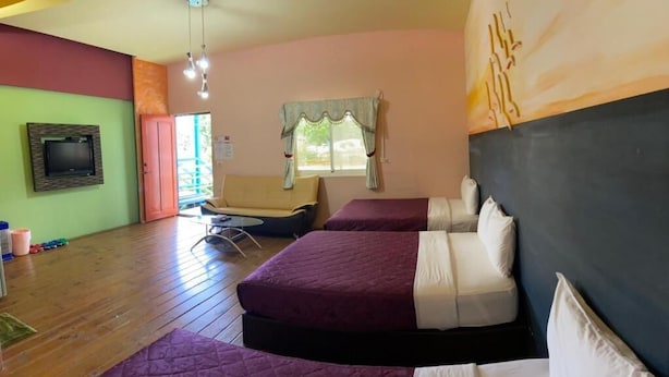 Quarto com duas camas, televisão na parede, janela com cortinas e uma pequena mesa com cadeiras.